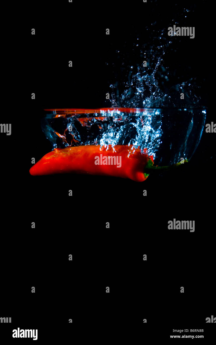 A Red Chilli falling into water with a black background Stock Photo - Alamy