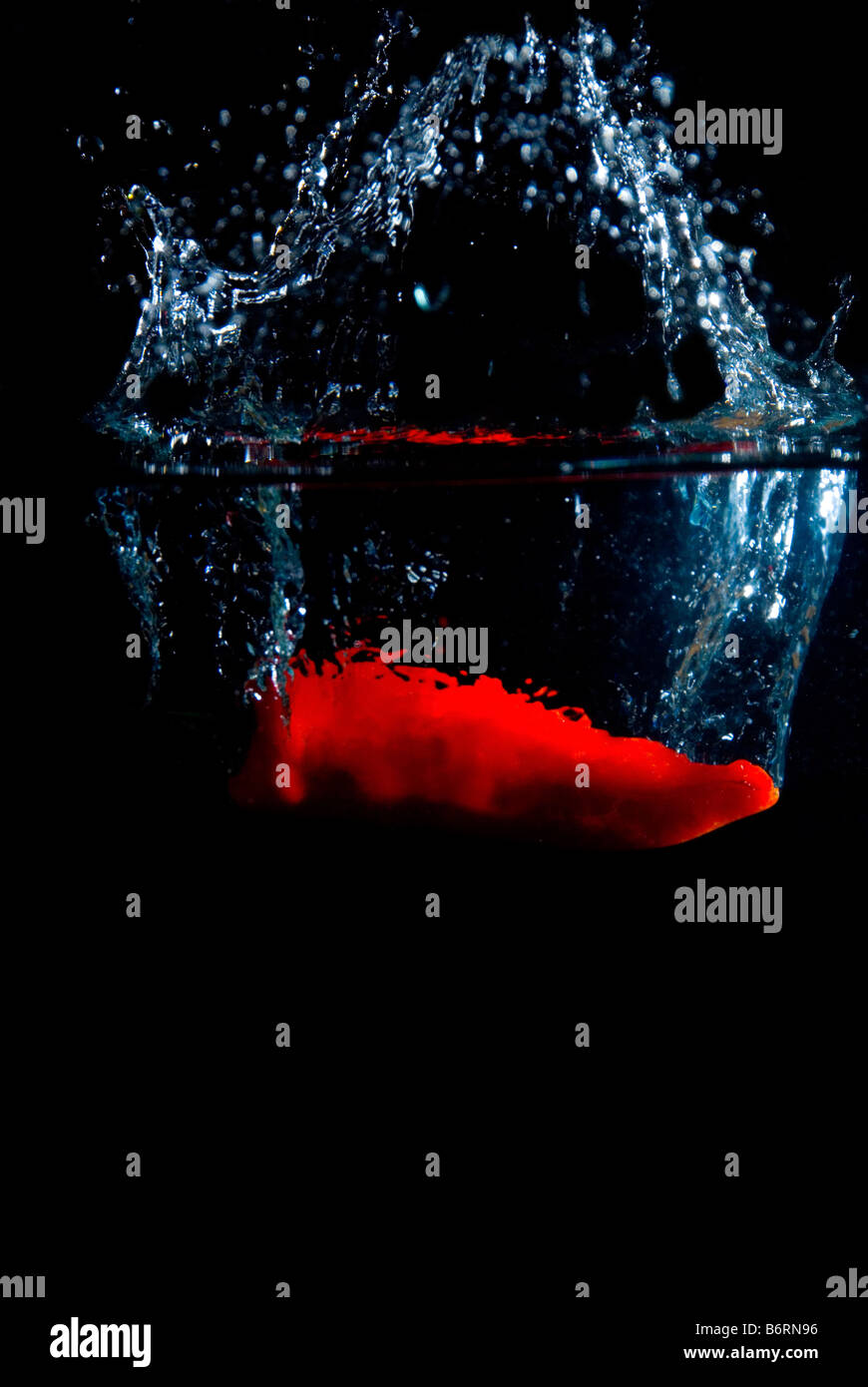 A Red Chilli falling into water with a black background Stock Photo - Alamy