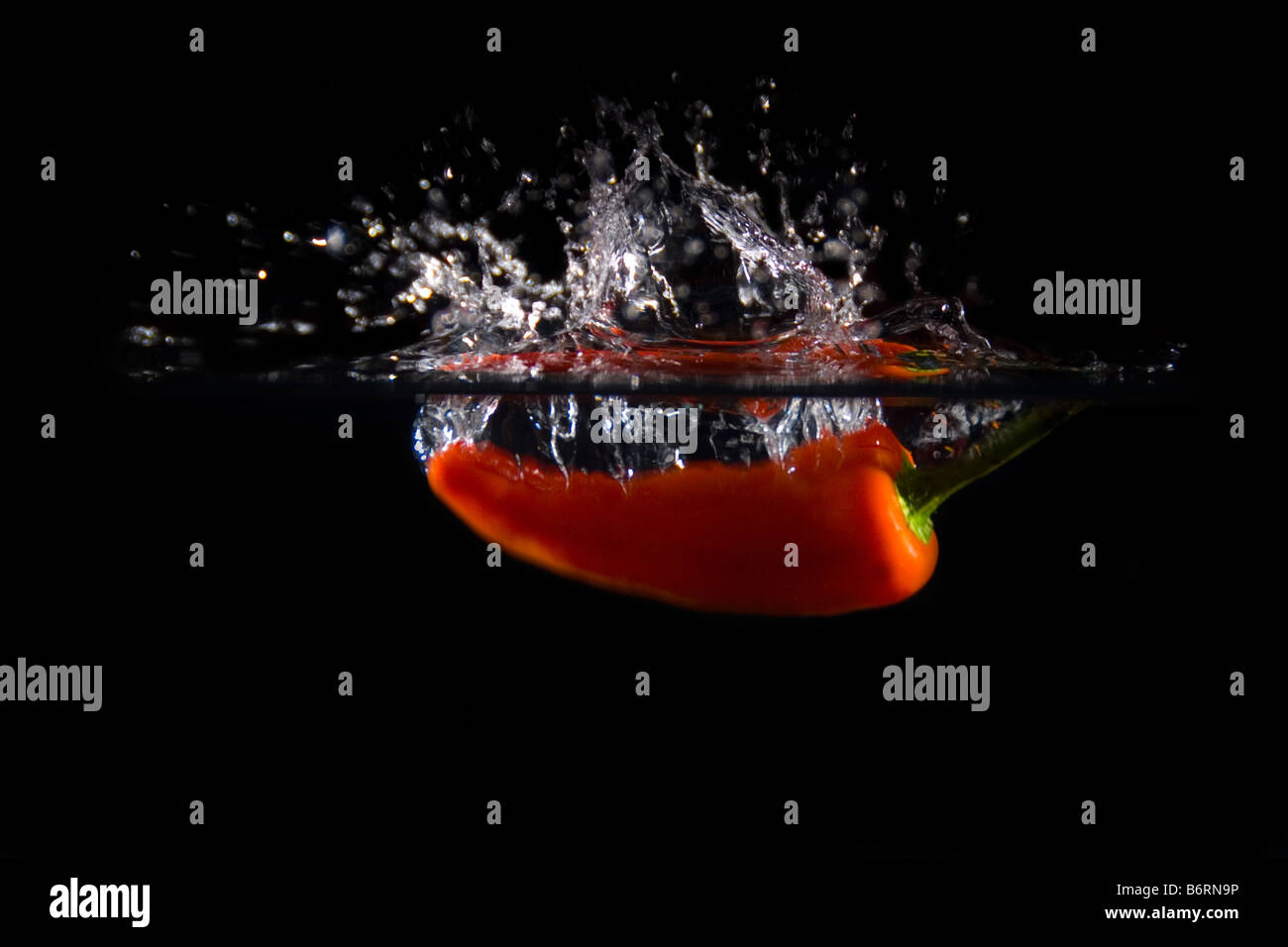 A Red Chilli falling into water with a black background Stock Photo - Alamy