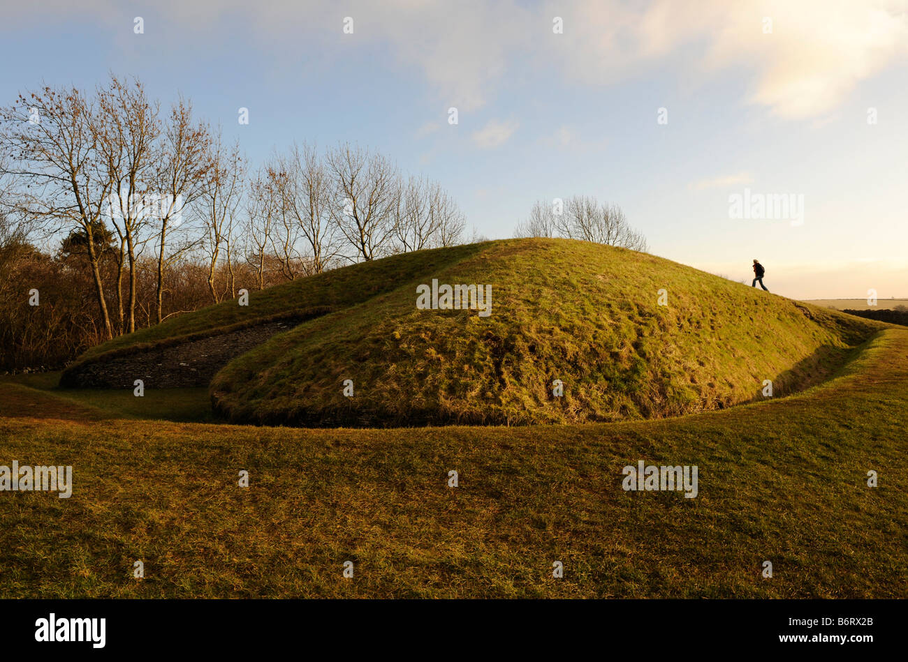 A walker passes the Stone Age long barrow of Belas Knapp near ...