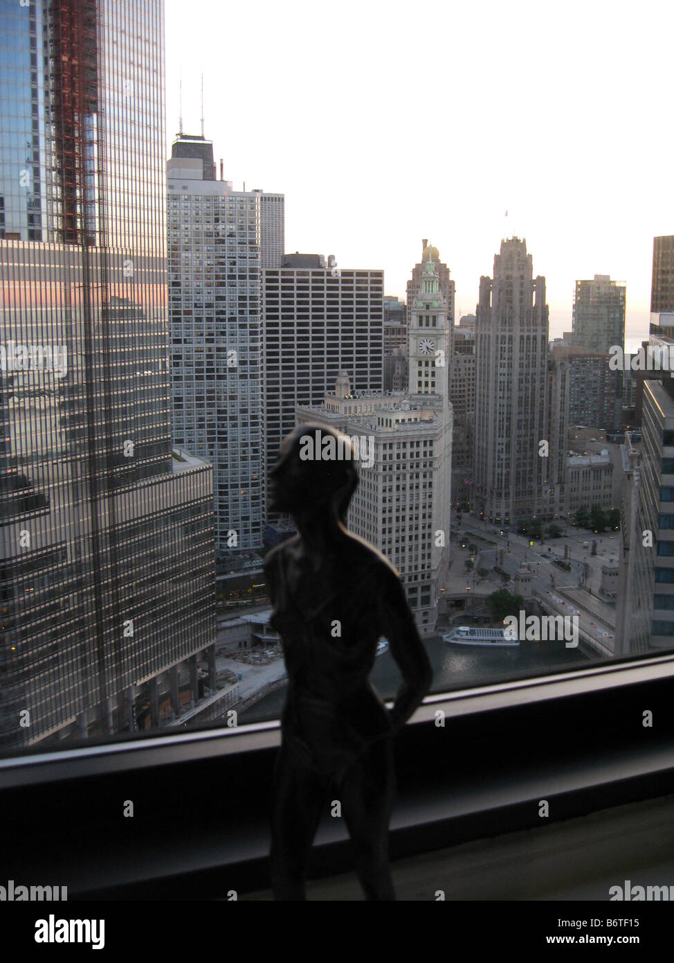 A small statue in front of a window in a skyscraper looking out with ...
