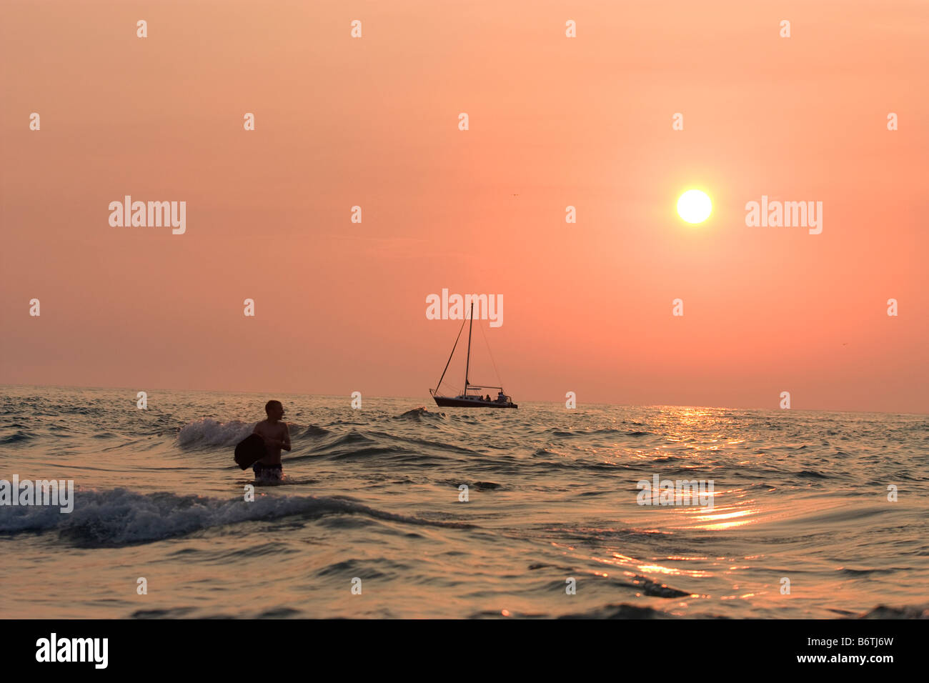 Boy playing in the surf at sunset with sailboat in background Stock ...
