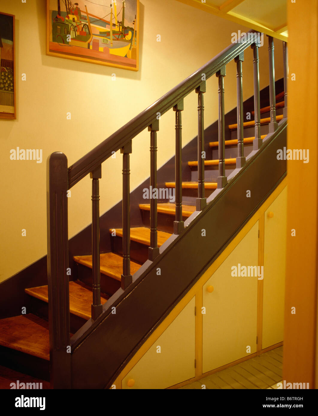 Fitted storage cupboards below staircase with dark wood bannisters in ...