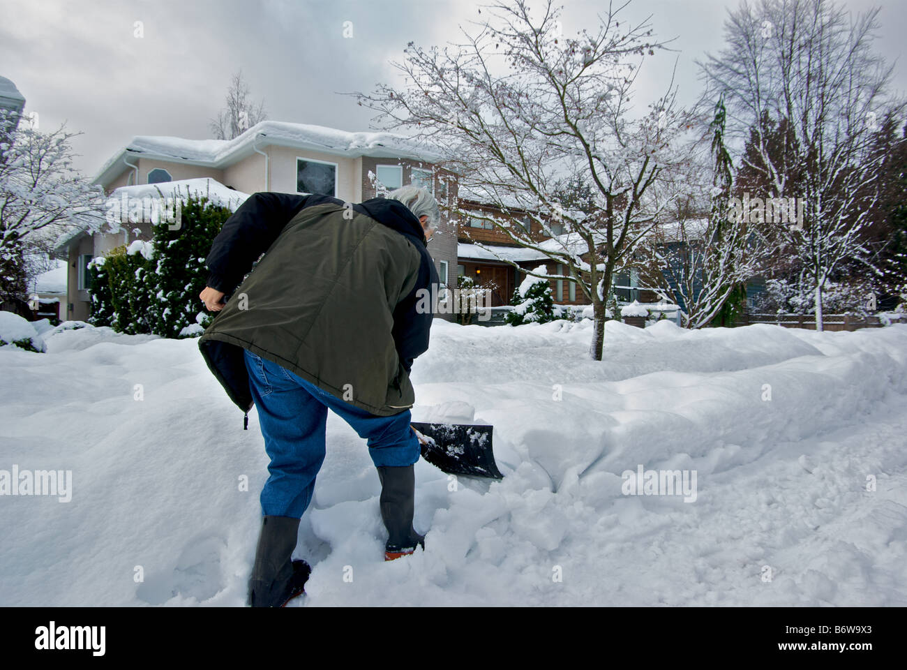 Man digging snow from edge of icy rutted road in front of house after ...