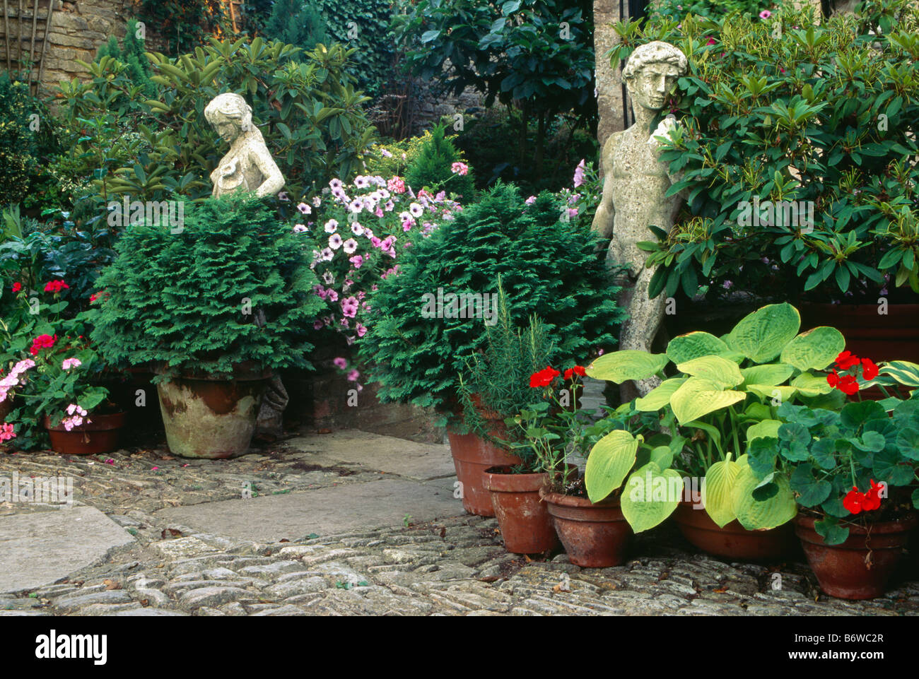 Classical statues on paved terrace with small conifers and red ...