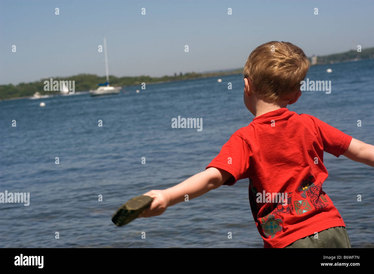 Young boy at seashore throwing rock into water Stock Photo - Alamy