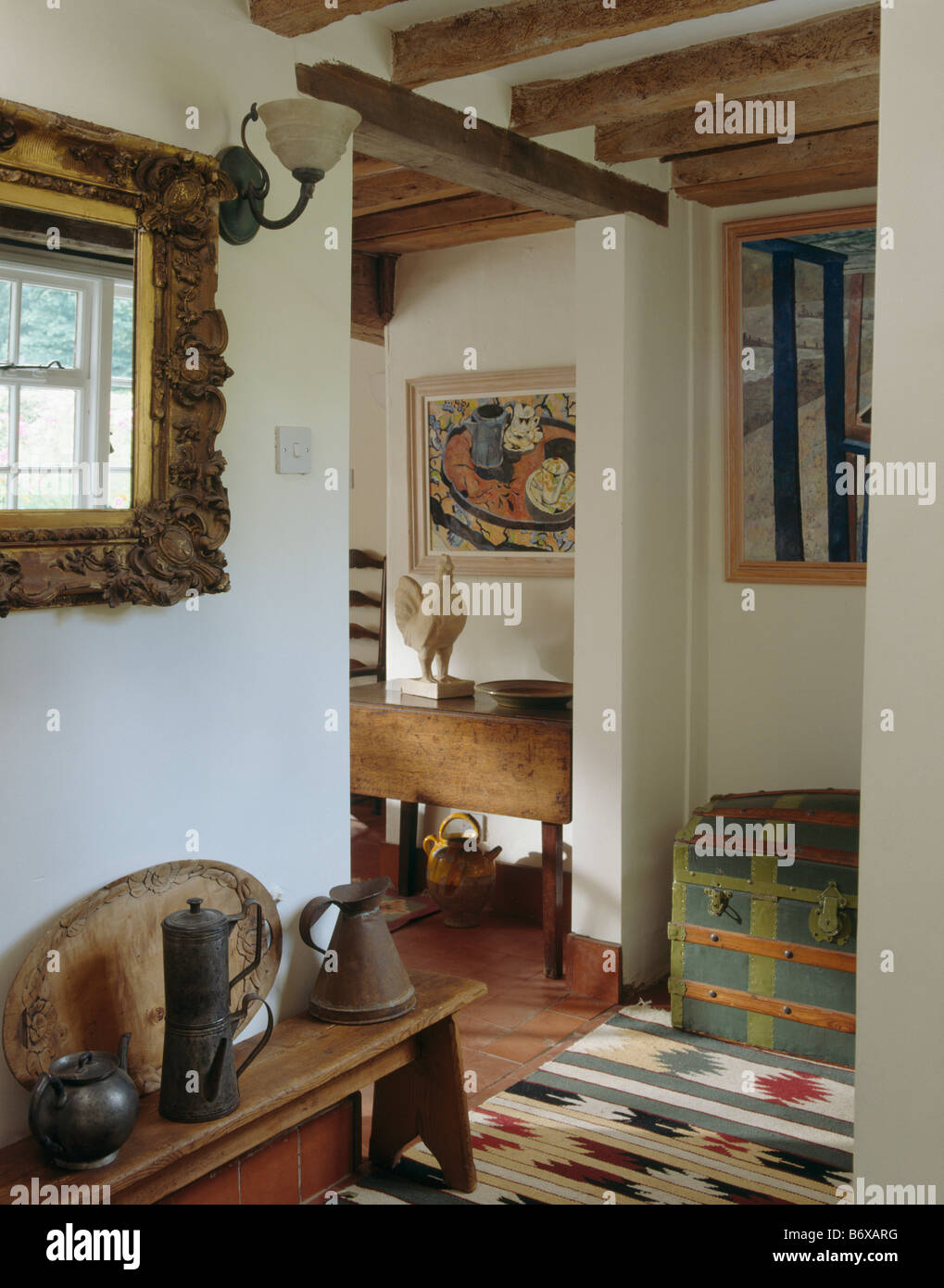 Ornate mirror above wooden bench with old pewter jugs in small cottage ...