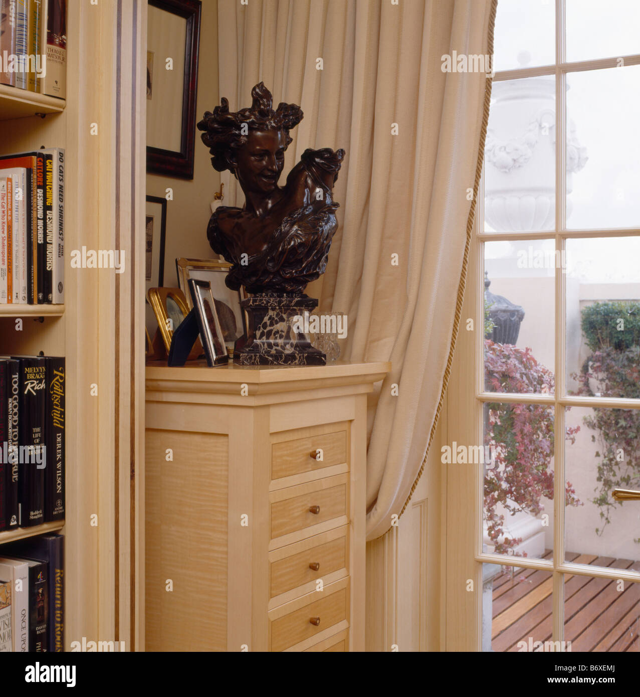 Bronze bust on narrow pale wood chest of drawers beside window with ...