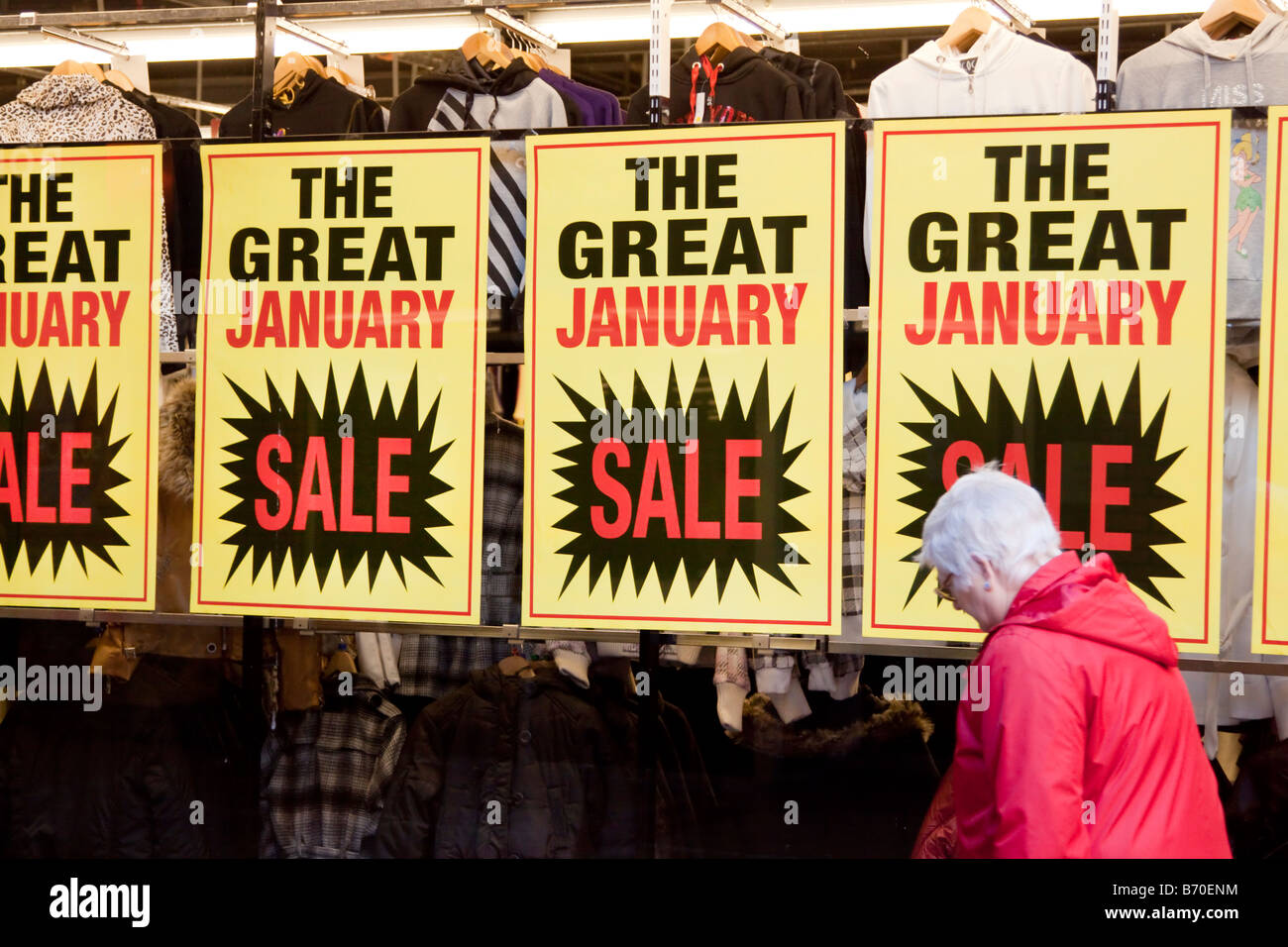 YELLOW JANUARY SALE SIGNS IN A SHOP WINDOW WITH A WOMAN SHOPPER WALKING ...