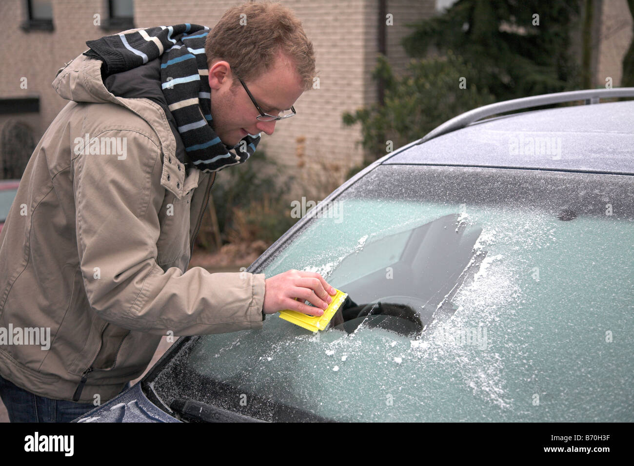 Student scraping windscreen clean of frost on a frosty winter morning ...