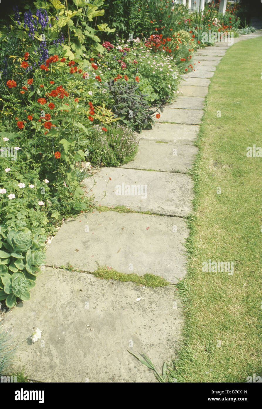Stone path between colourful summer flowering border and lawn in ...