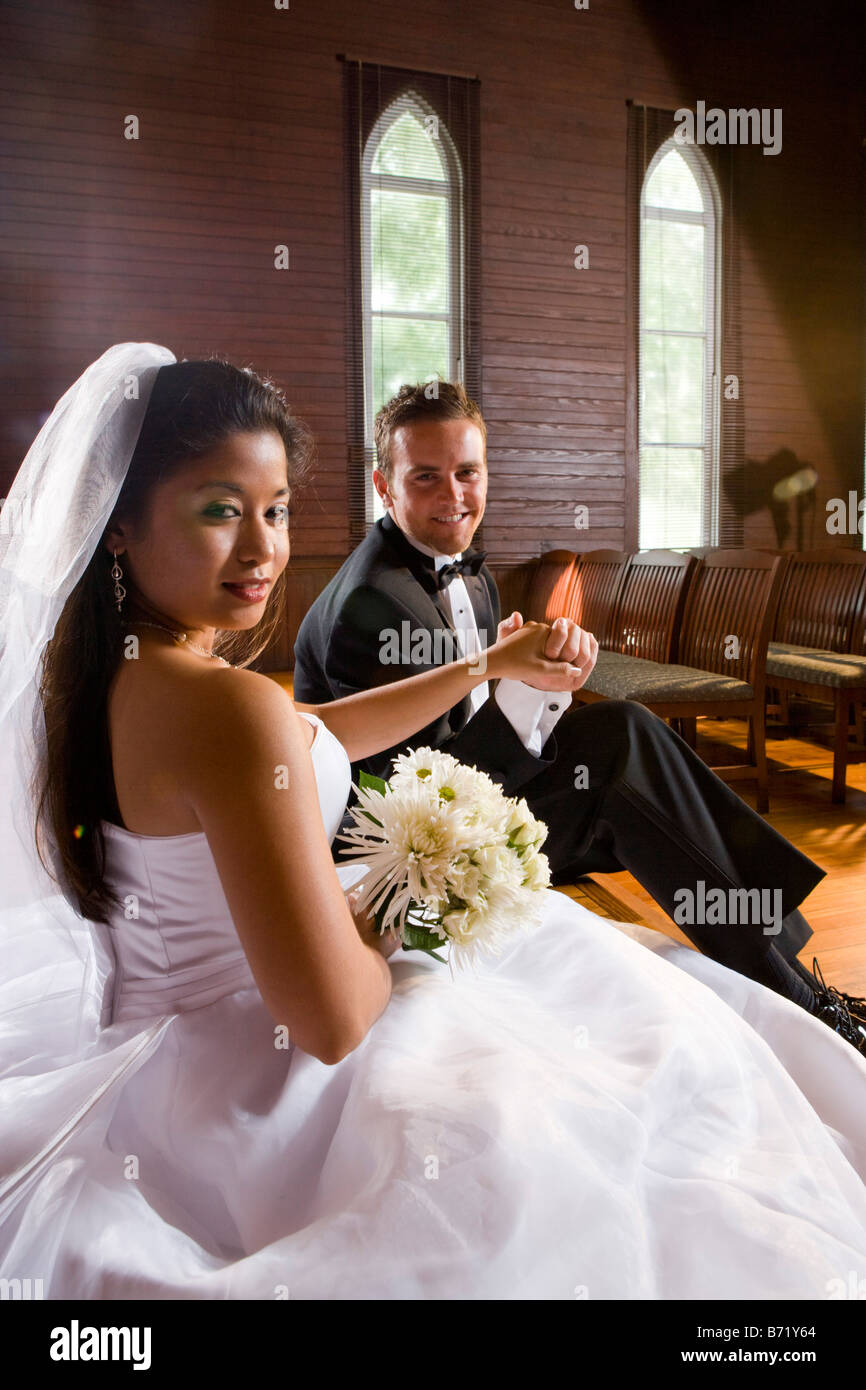 Young interracial bride and groom sitting on wooden altar of church on ...
