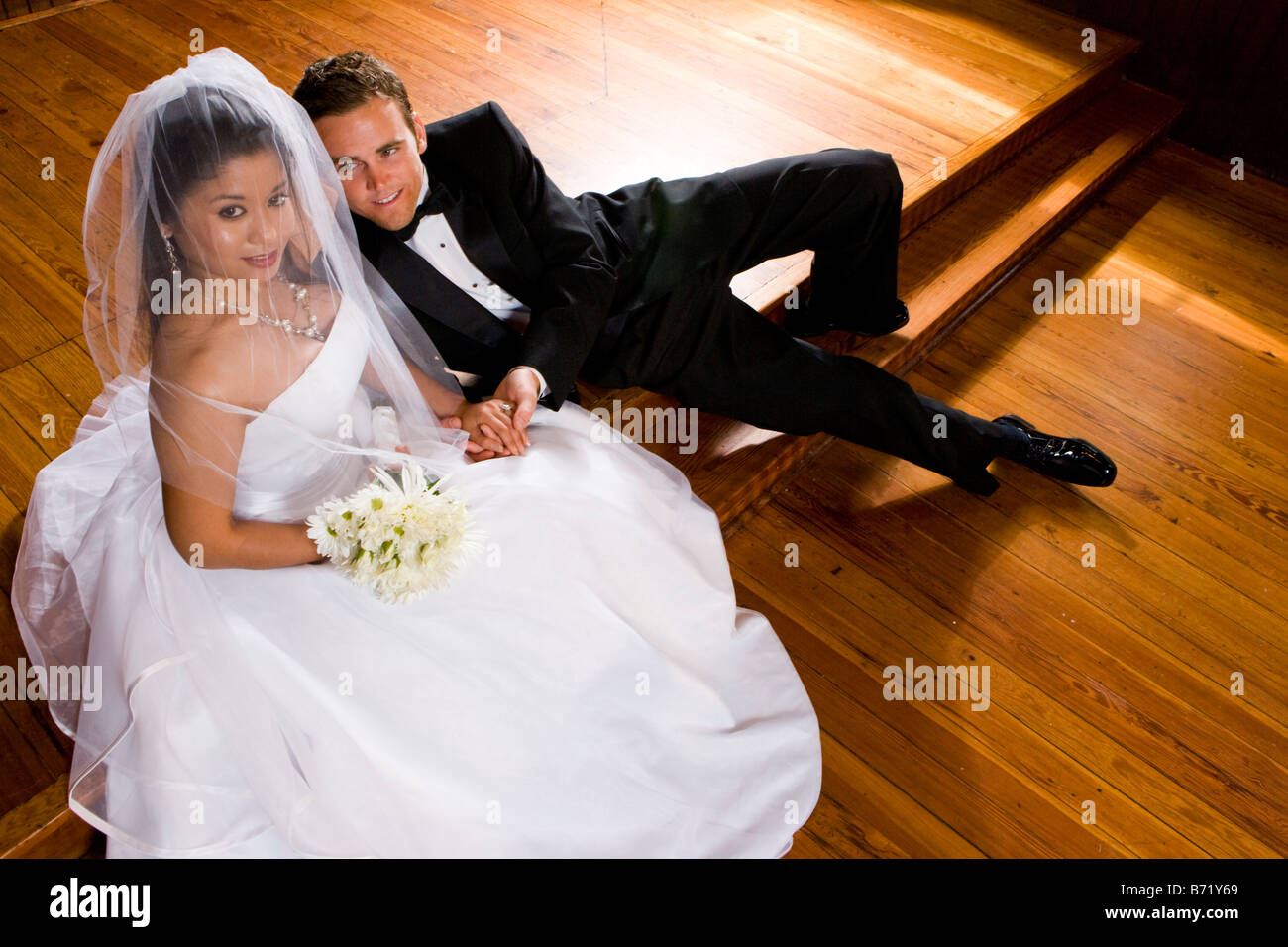 Young interracial bride and groom sitting on wooden altar of church on ...