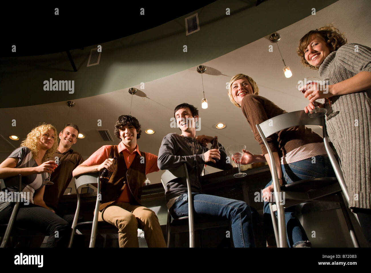 Low angle portrait of friends sitting at bar drinking and hanging out ...