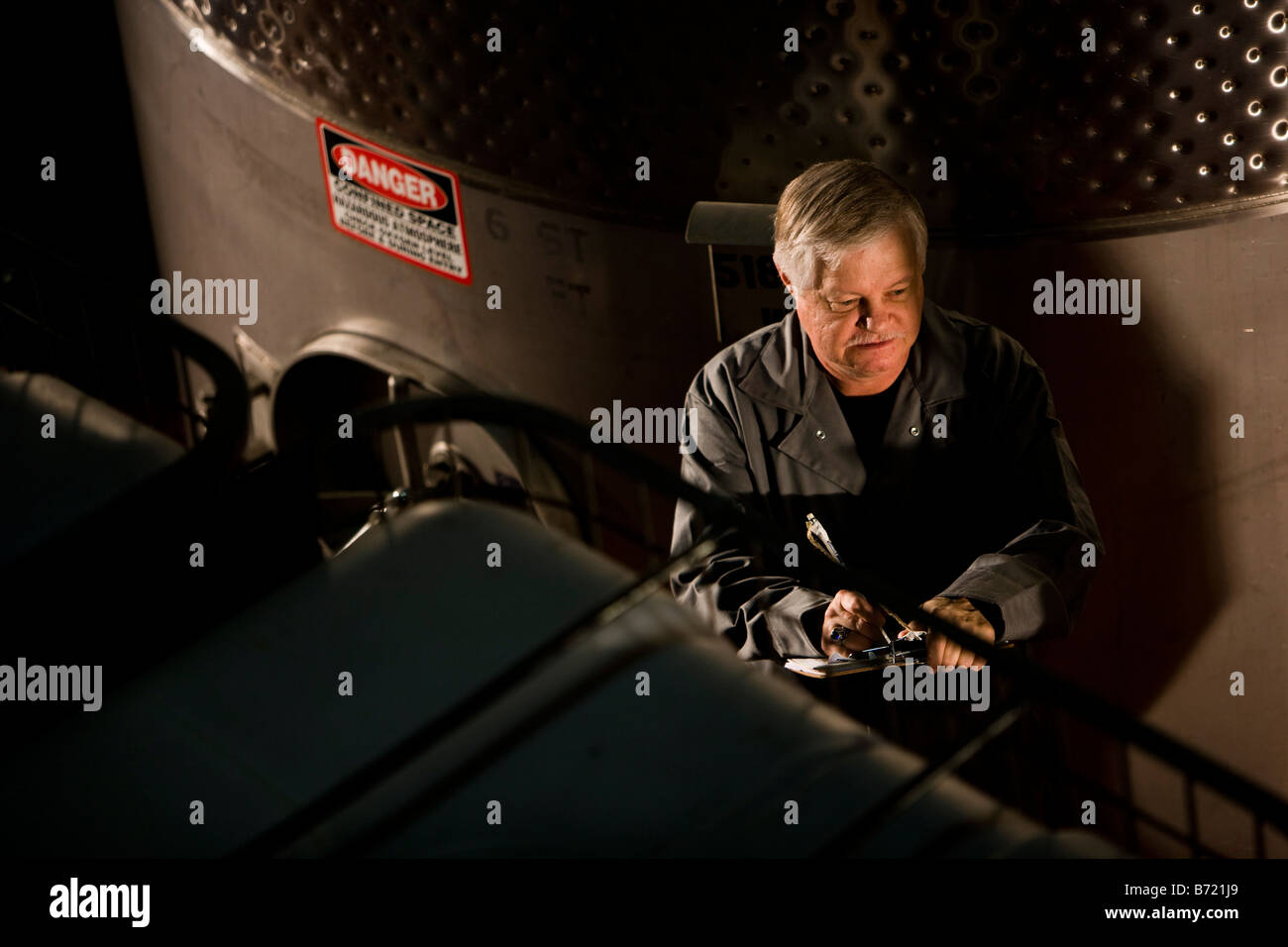 Blue-collar worker in factory next to storage tanks Stock Photo - Alamy