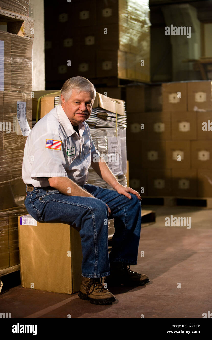 Male worker sitting on a box in a storage warehouse Stock Photo - Alamy