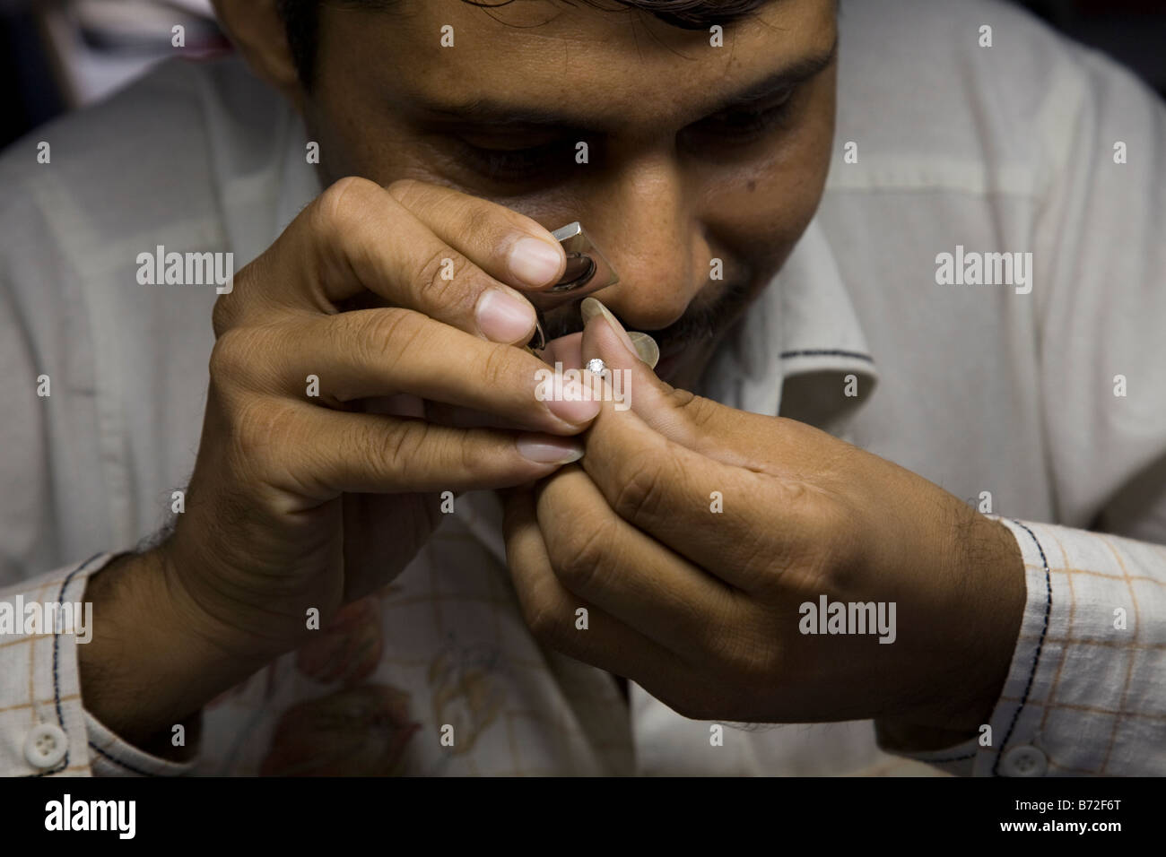 Diamond worker looks through a magnifying lens at a diamond he is ...
