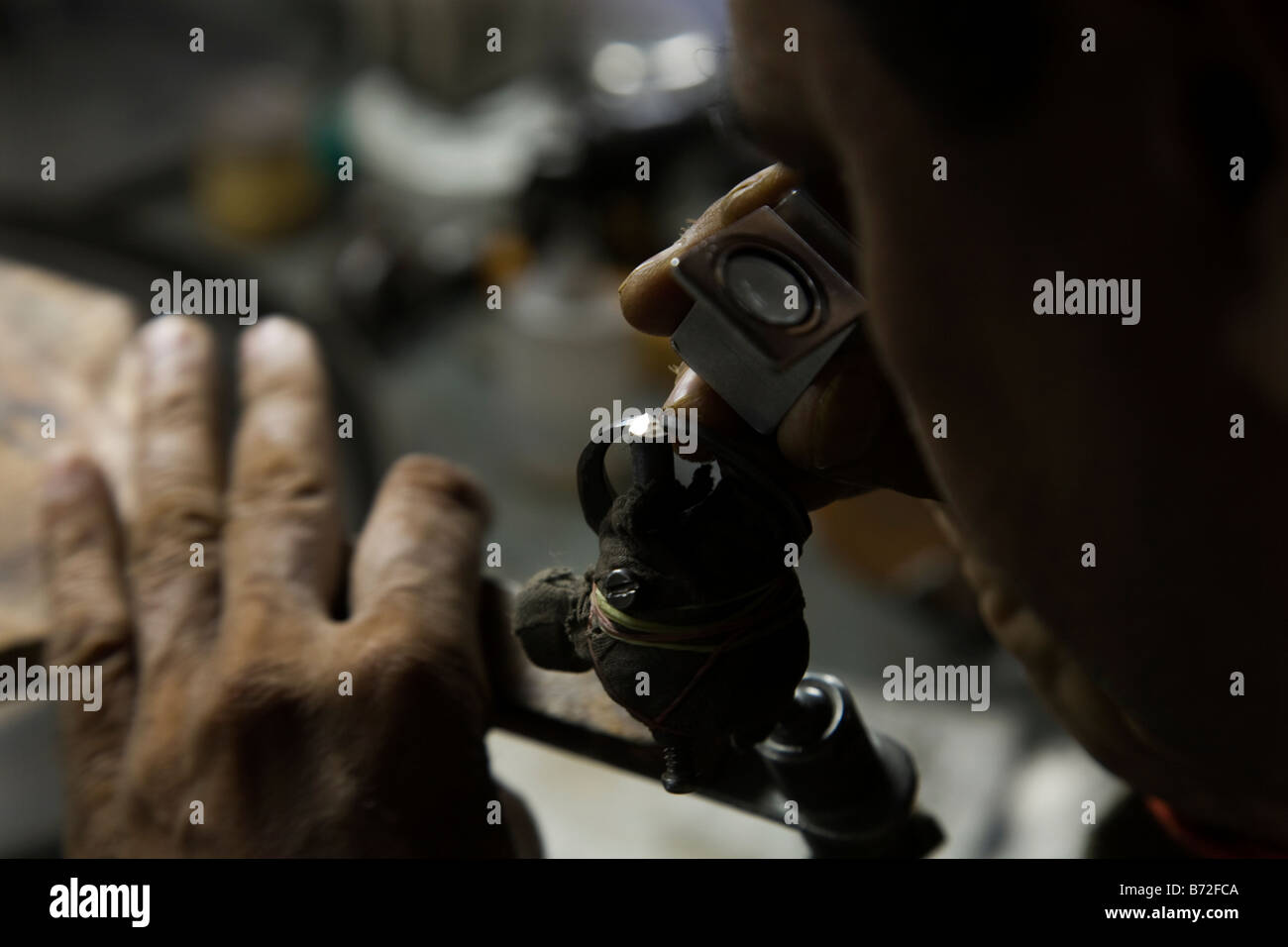 Diamond worker looks through a magnifying lens at a diamond he is ...