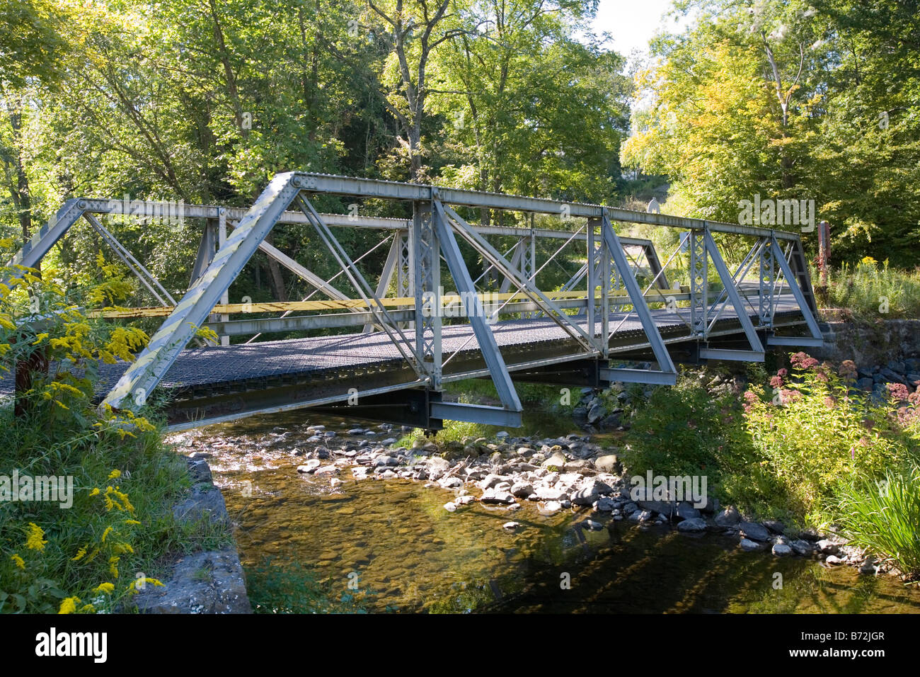 A lonely view of a country metal bridge with a flowing creek underneath ...