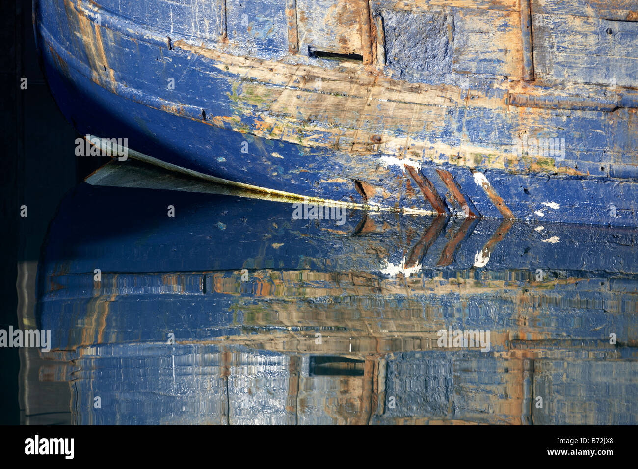 blue painted weathered hull of fishing boat reflecting in calm water ...