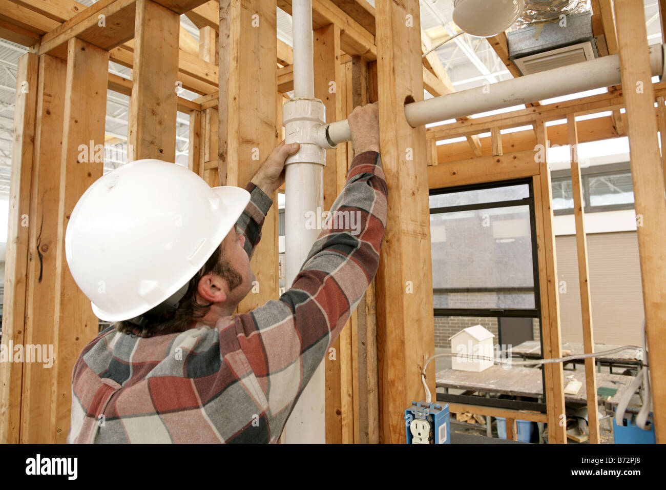 A construction worker connecting plumbing pipe in an unfinished wall ...