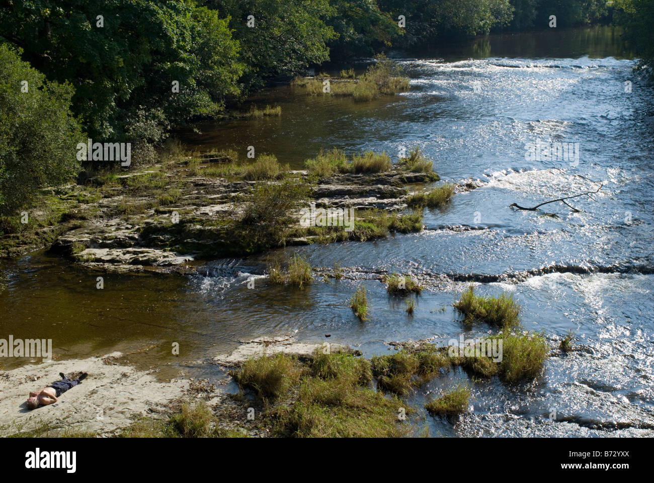 A man sleeping in the sun on rocks beside the River Severn in Newtown ...