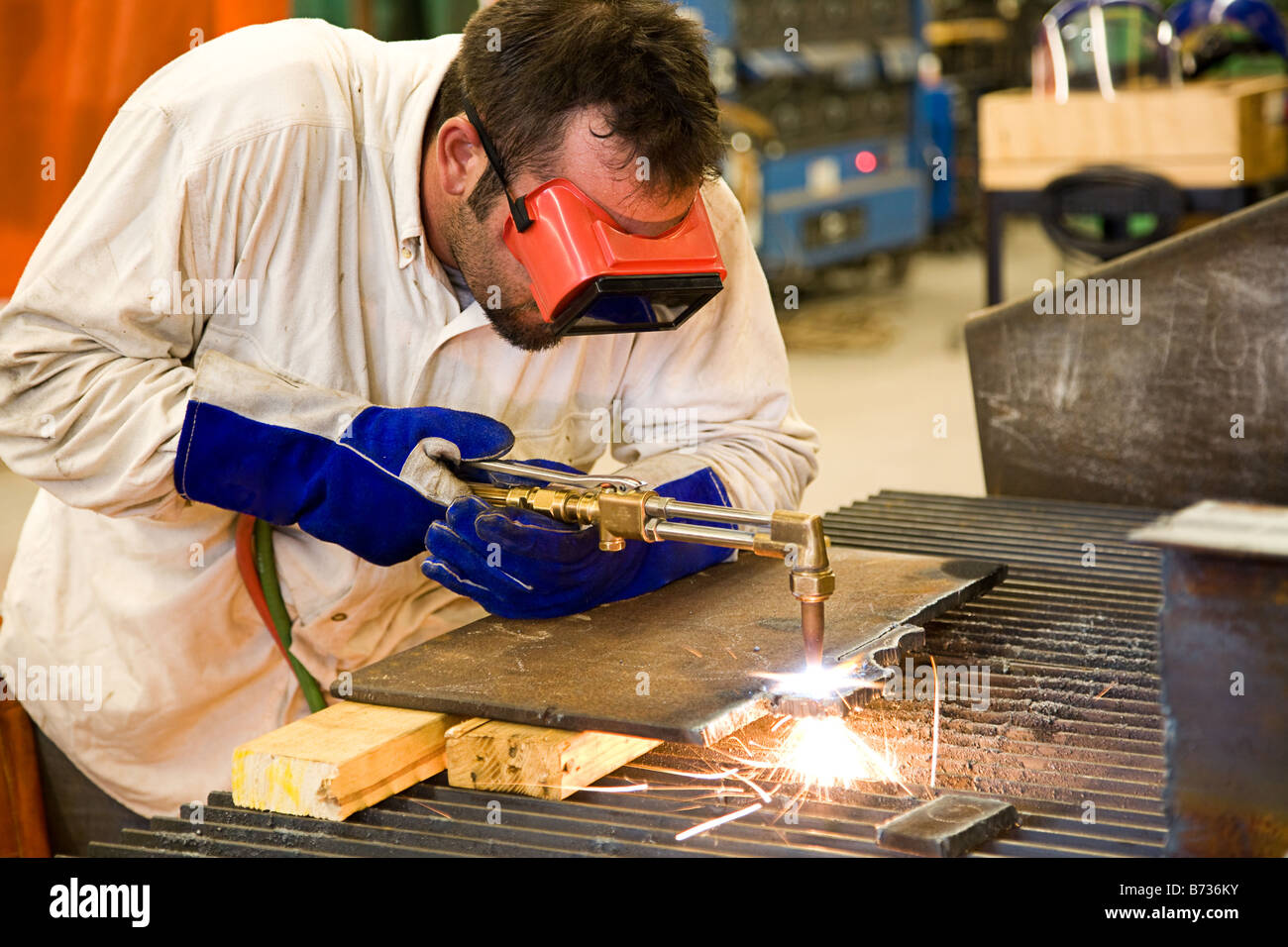 Worker using an acetylene torch to cut through metal in a metalworks ...