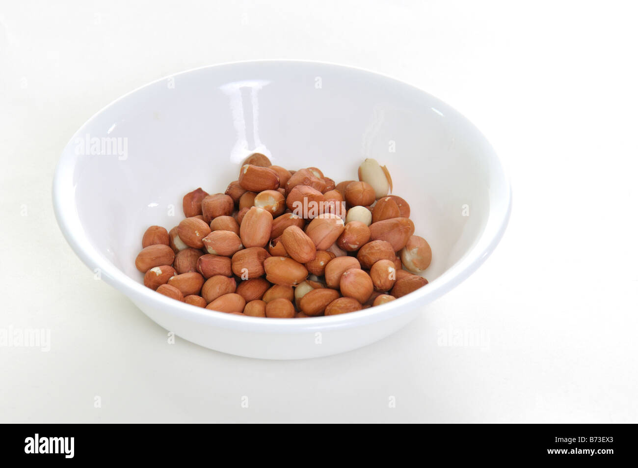 a small white bowl of raw peanuts on a white background Stock Photo - Alamy
