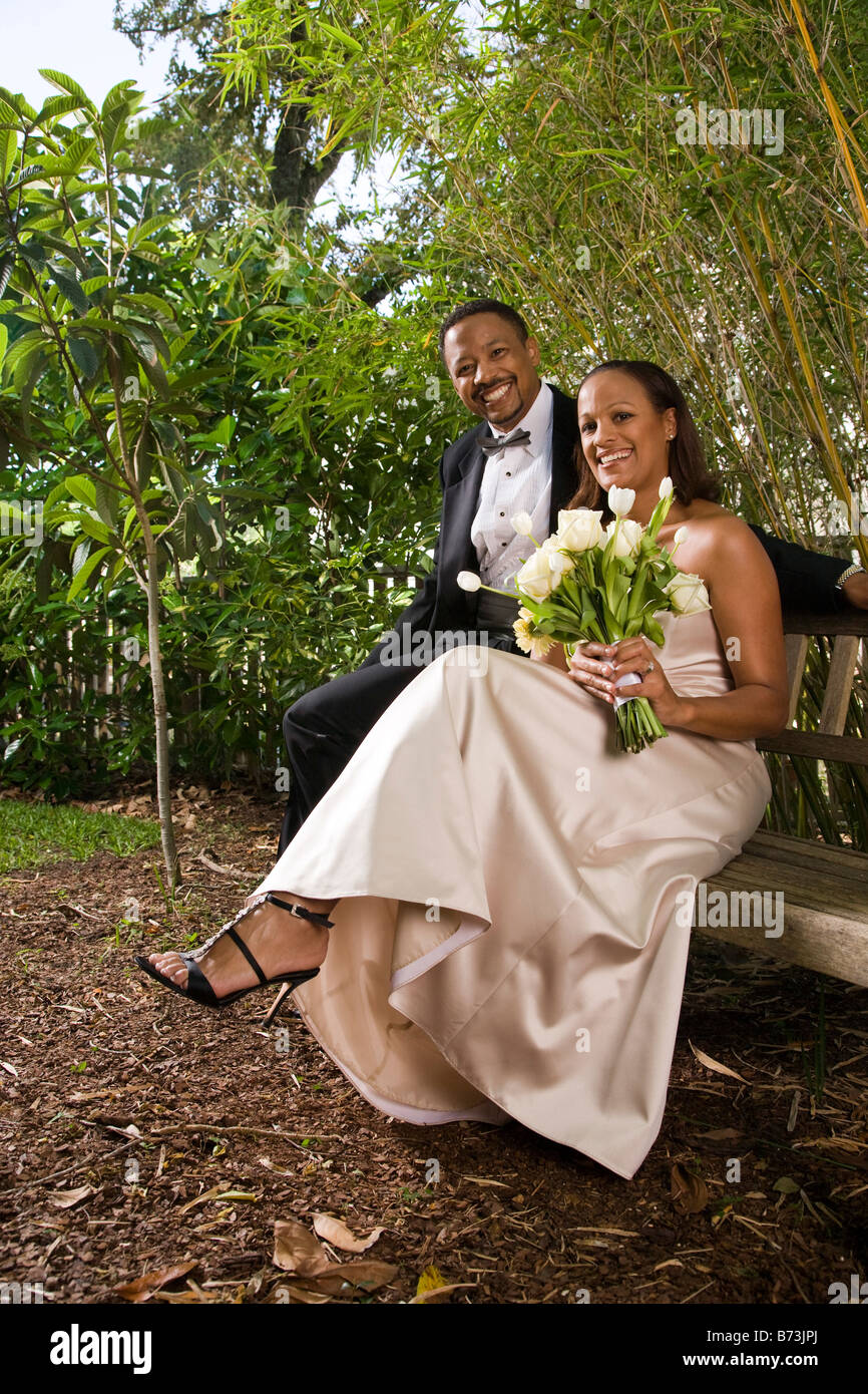 Happy African-American bride and groom on bench outdoors on wedding day ...