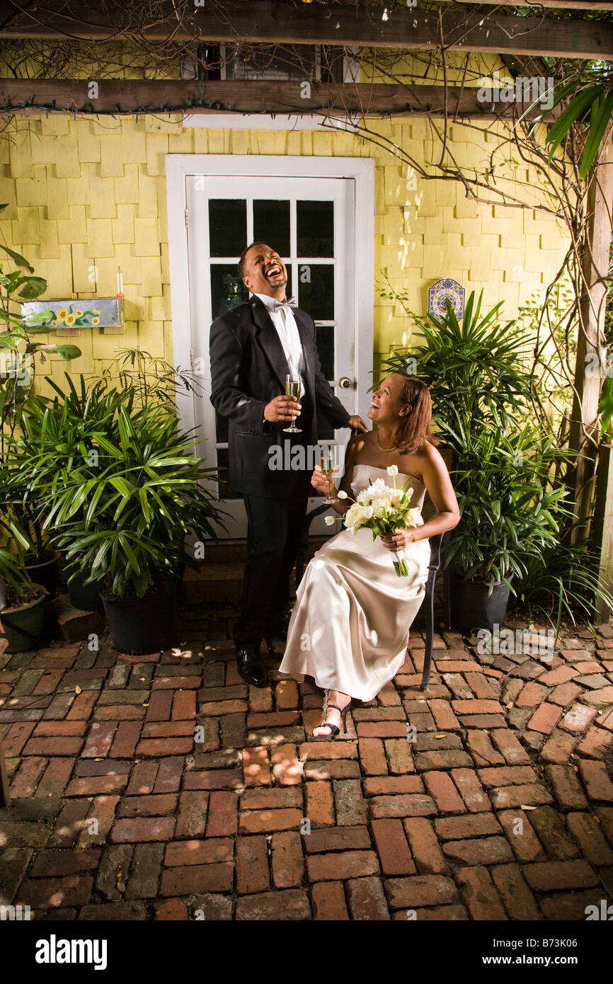 African-American bride and groom laughing, drinking champagne on patio ...