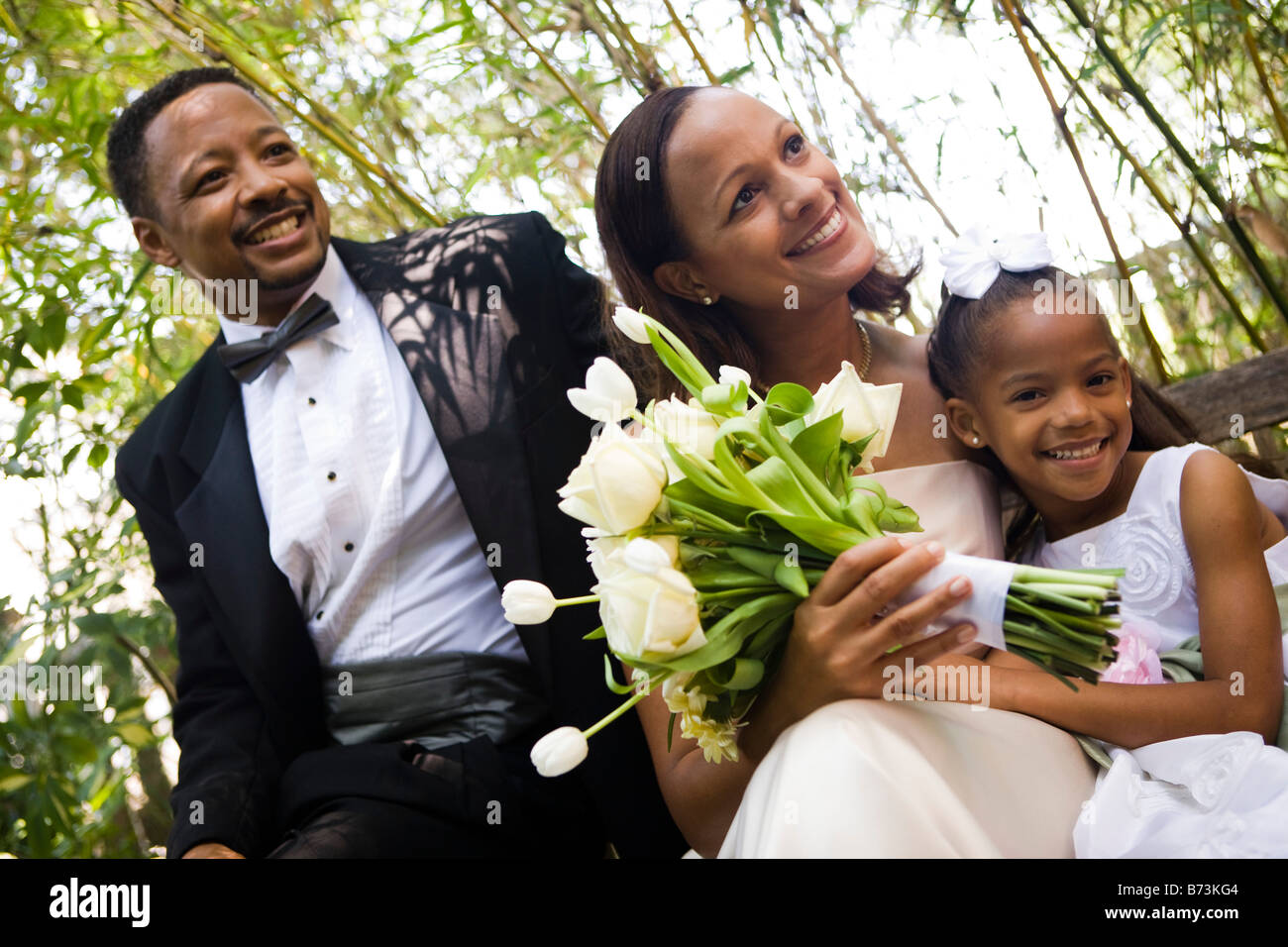 Happy African-American bride and groom sitting outside with flower girl ...