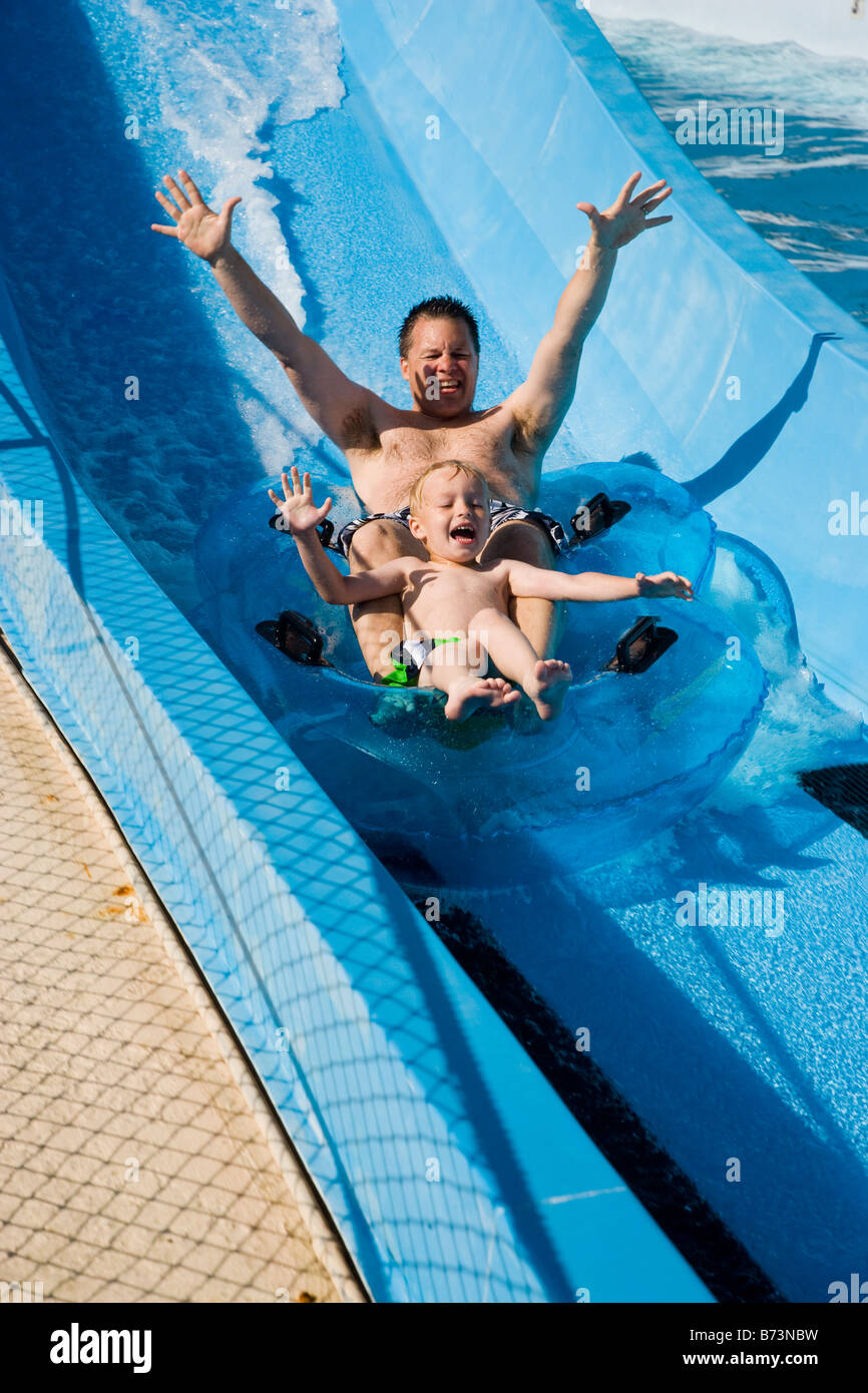 Father And Son Sliding Down Water Slide Together On Innertube In Water