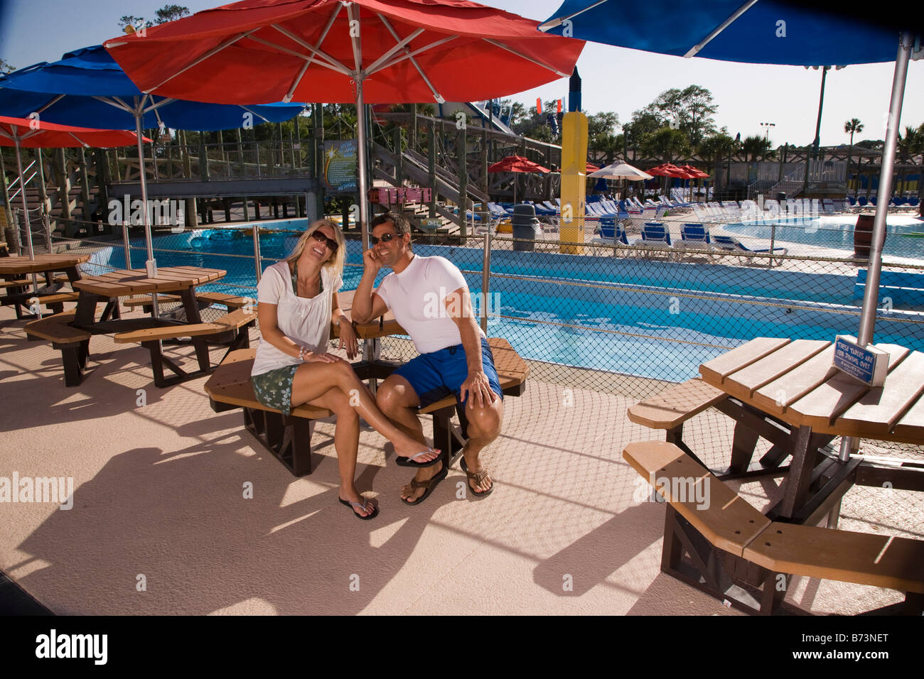 Mid-adult couple sitting at picnic table by pool Stock Photo - Alamy