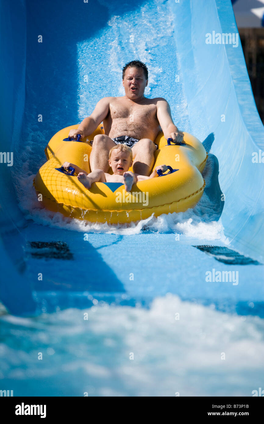 Father and son sliding down water slide together on innertube in ...
