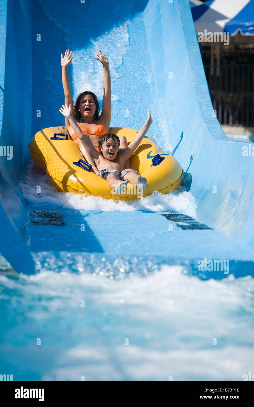 Mother And Son Sliding Down Waterslide Together On Innertube In Water