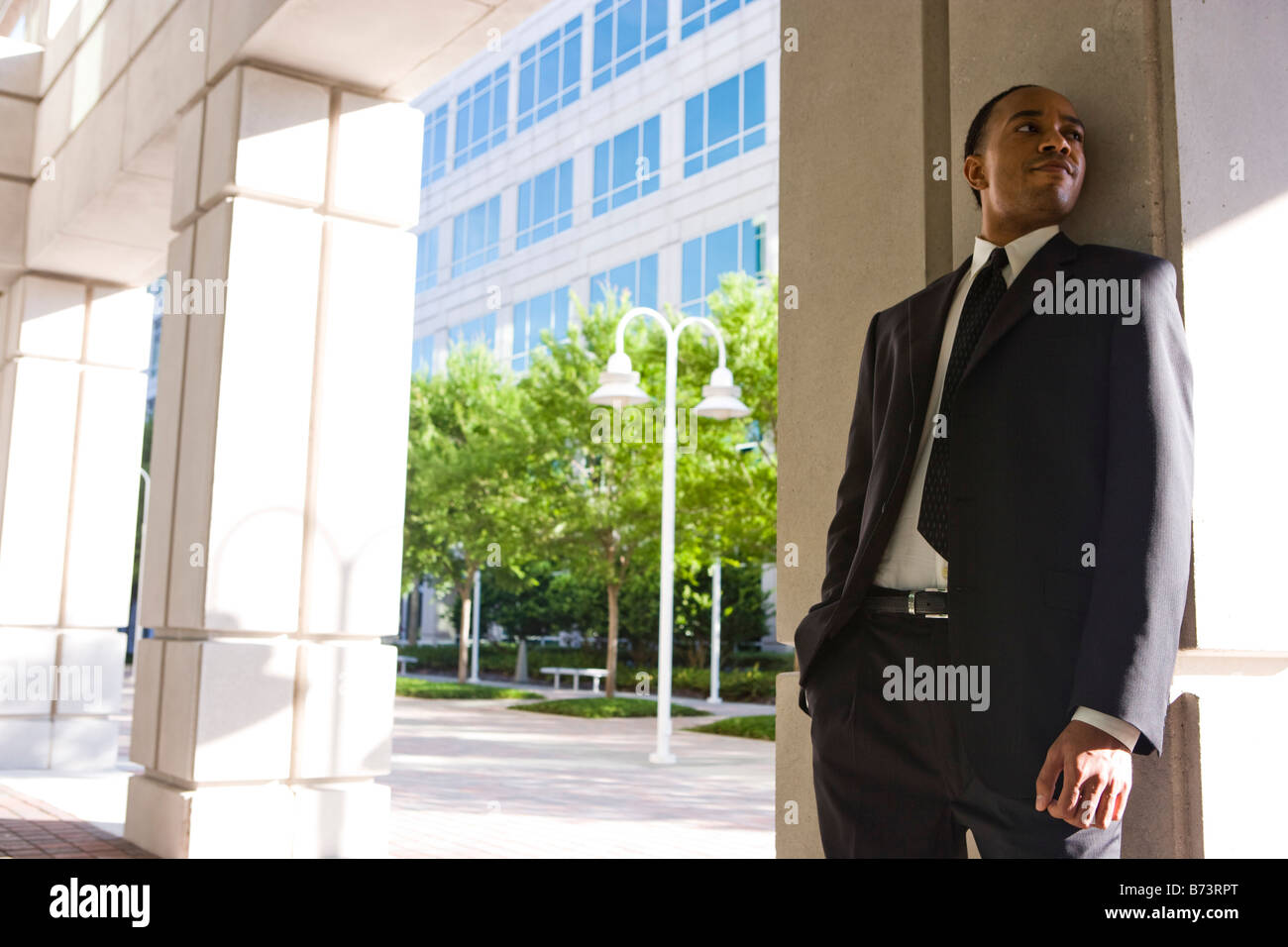 Businessman leaning against wall with office building in background ...
