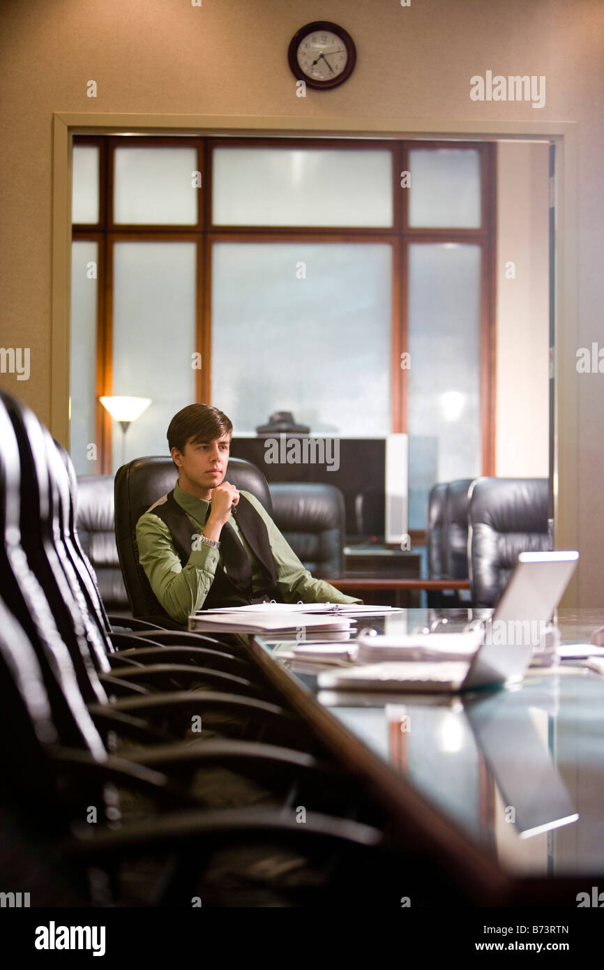 Young office worker sitting in conference room beside long row of empty ...