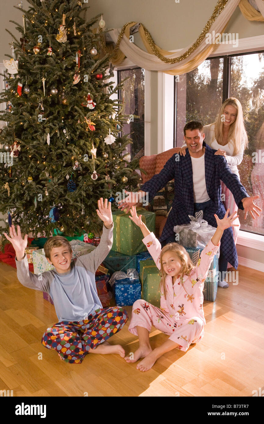 Young happy family sitting in front of Christmas tree Stock Photo - Alamy