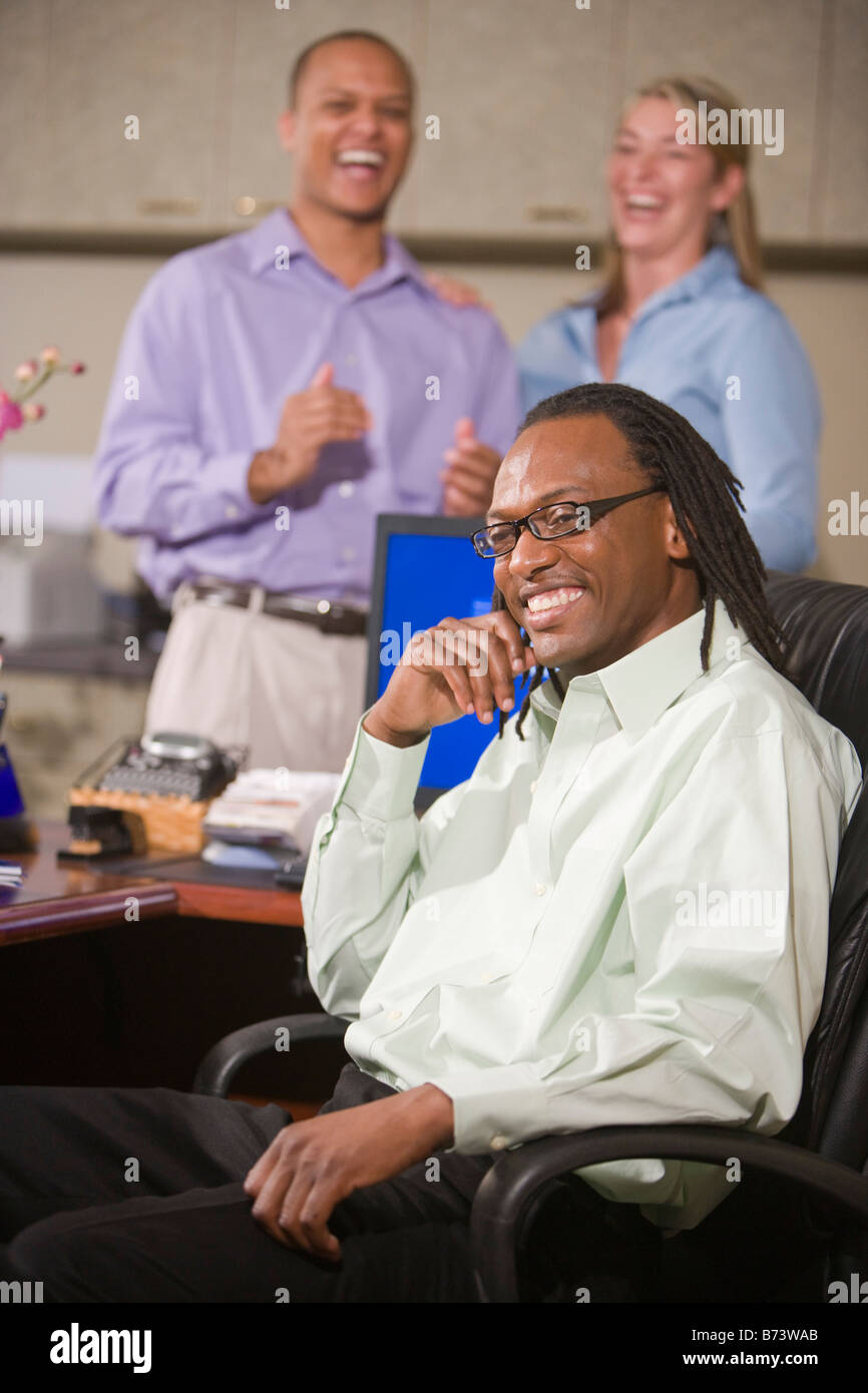 African-American office worker at desk, co-workers in background Stock ...
