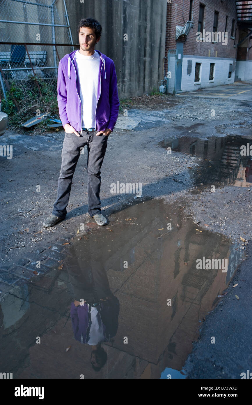 Young man standing in run-down alleyway in front of puddle Stock Photo ...