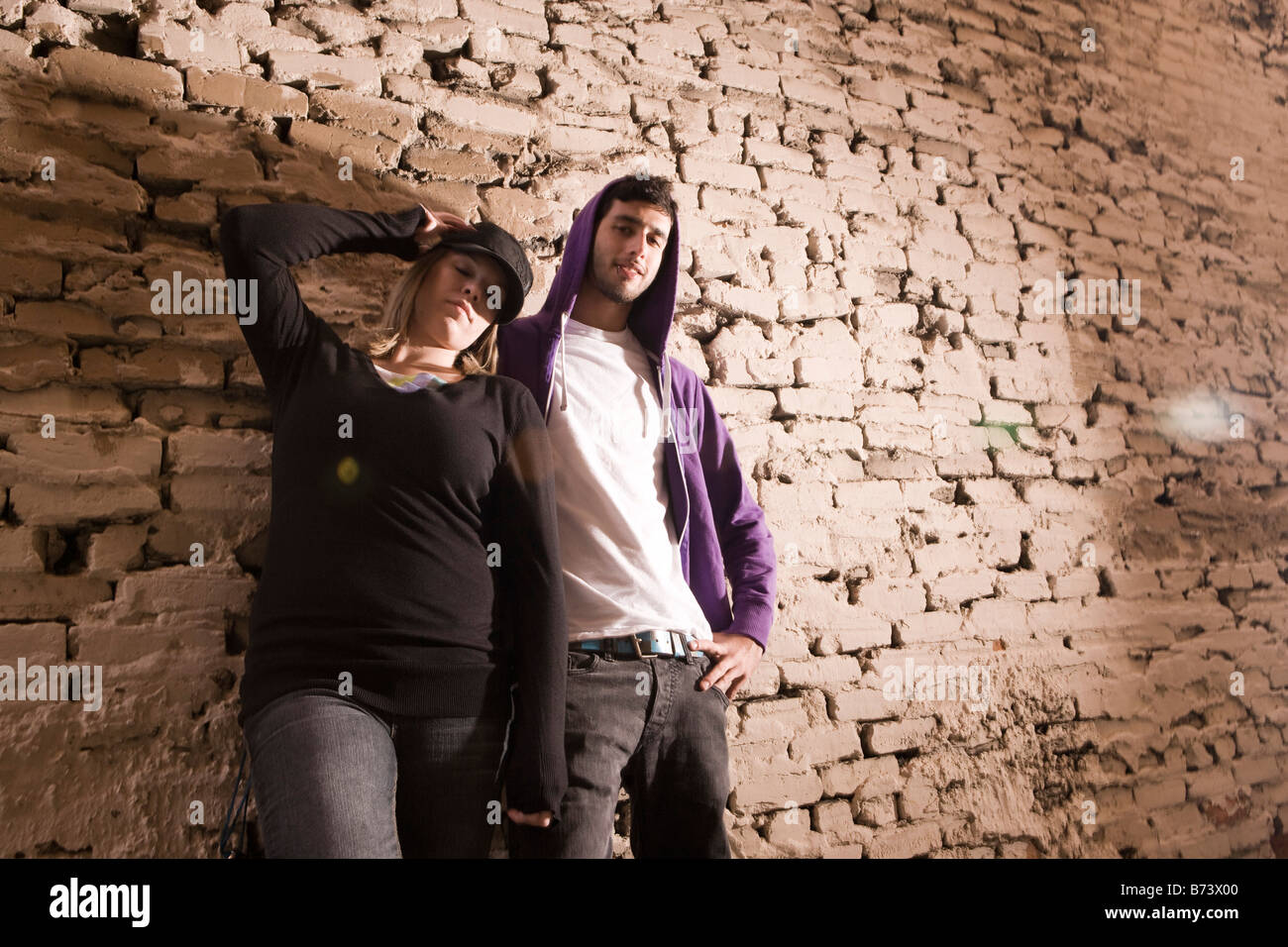 Portrait of young couple hanging out outside in front of brick wall ...