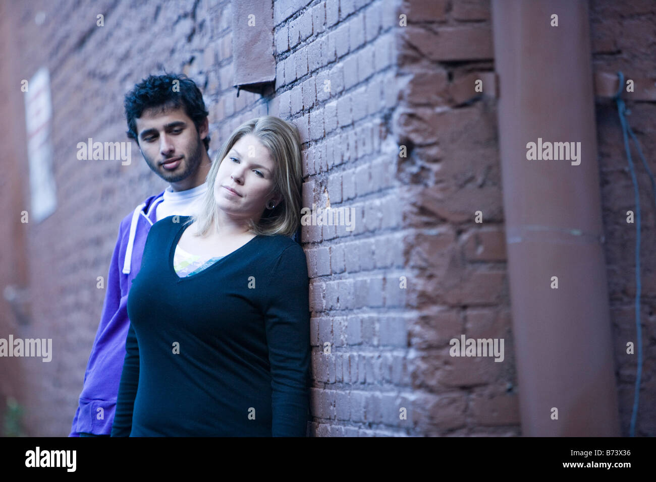 Young couple leaning up against brick wall of building outside Stock ...