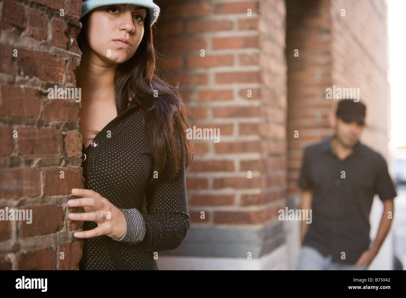 Young woman looking out behind brick wall, man approaching in ...
