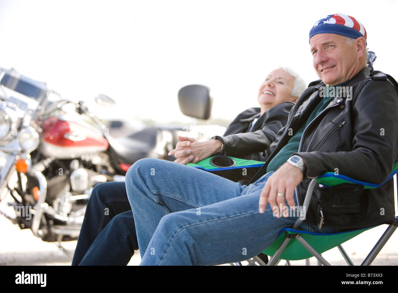 Happy senior biker couple sitting on chairs next to motorcycle Stock ...
