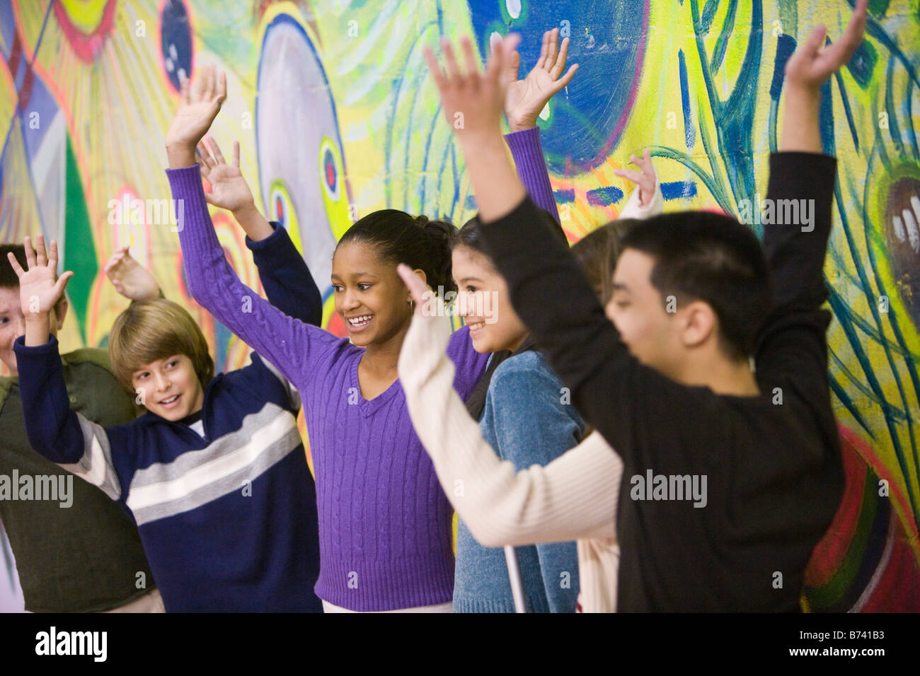 Multi-ethnic children with arms raised in front of artwork mural wall ...
