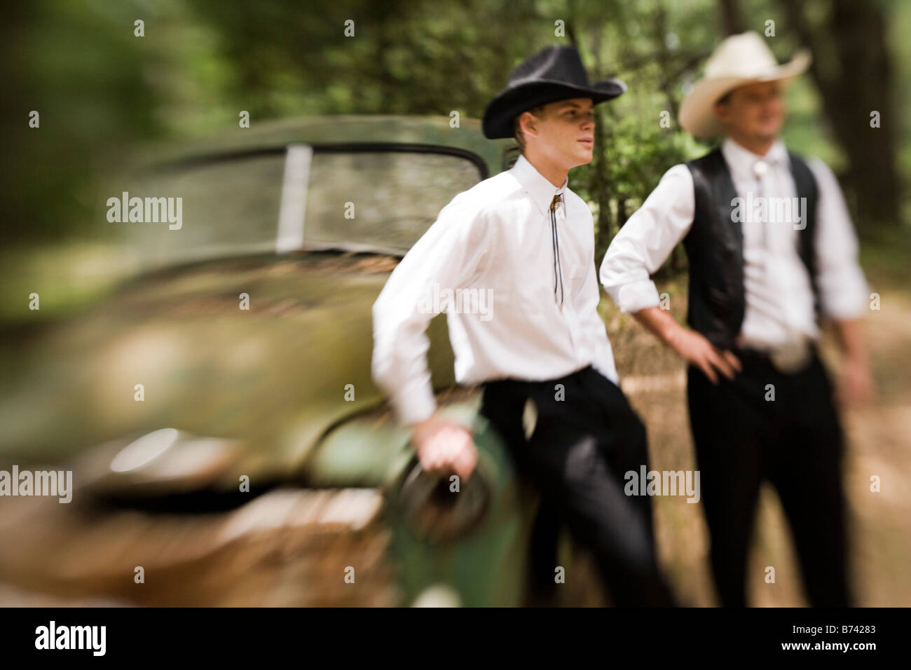 Two young men wearing cowboy hats and Western formalwear leaning on old ...