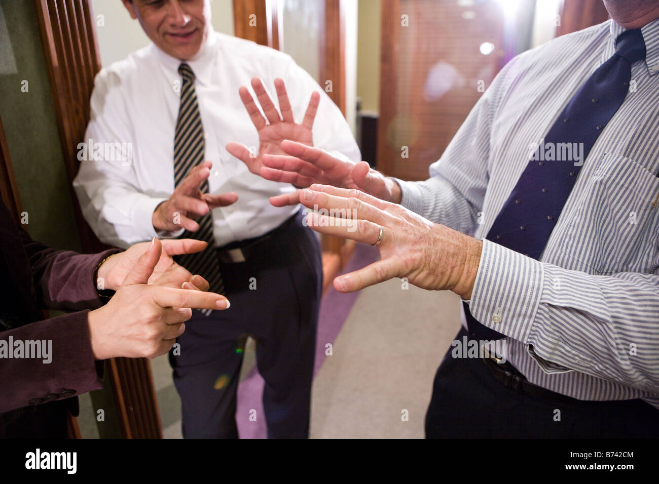 Midsection of three businesspeople having discussion in office corridor ...