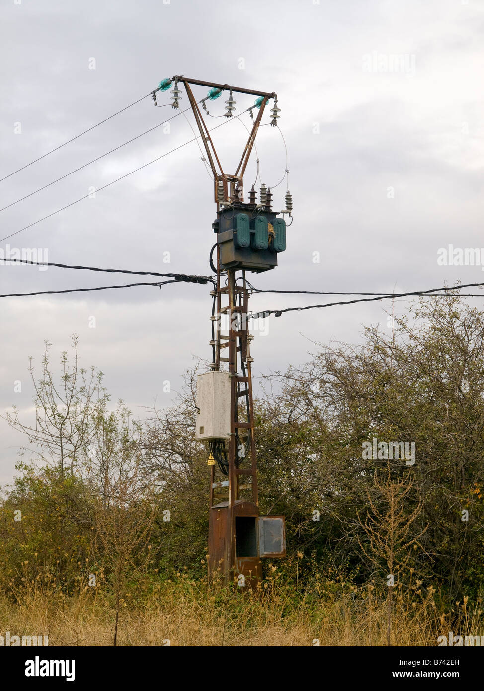 High voltage electric pillar in forest against clouds, with low current ...