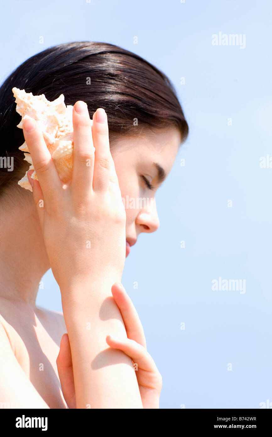 Young woman holding conch shell to ear eyes closed portrait Stock Photo ...