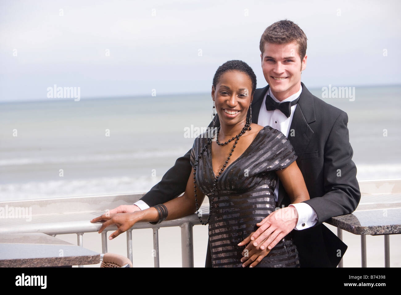 Young interracial couple wearing tux and black dress posing at beach Stock Photo - Alamy